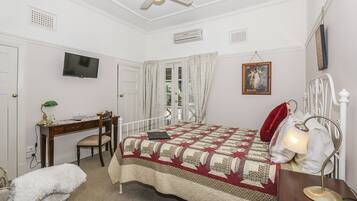 Um quarto com cama, escrivaninha, cadeira, luminária e televisão.