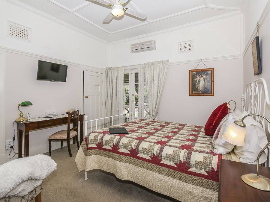 Um quarto com cama, escrivaninha, cadeira, luminária e televisão.