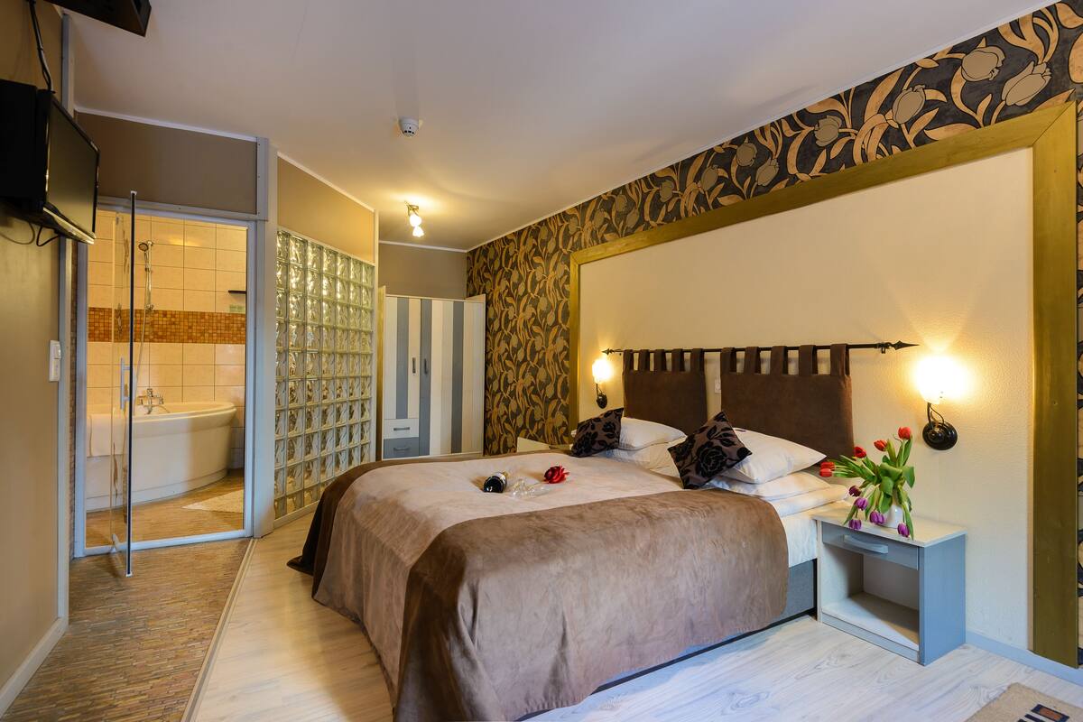 Quarto com cama grande, mesa de cabeceira com um vaso de flores, área de chuveiro e banheiro com banheira.
