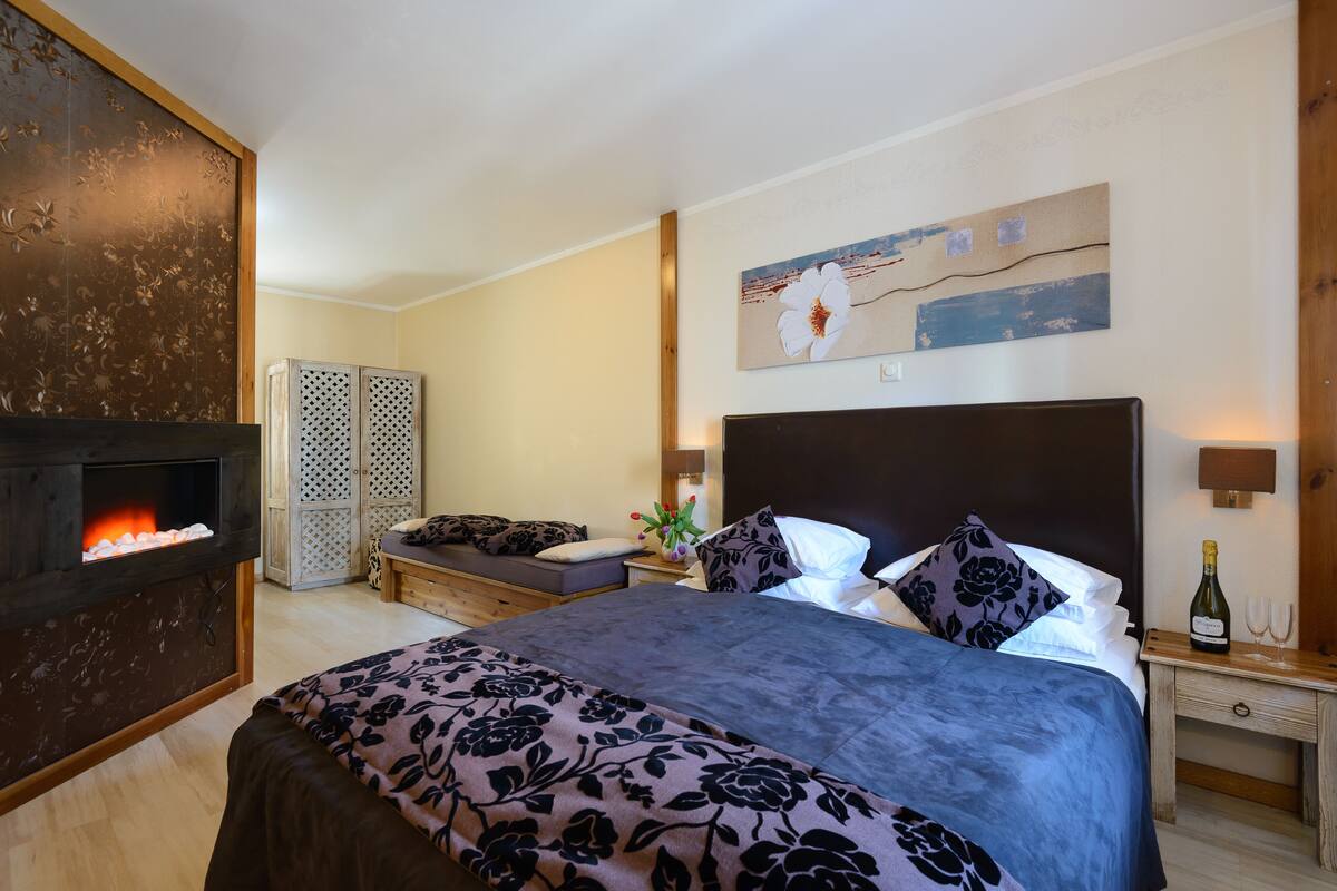 Quarto com cama, armário de madeira com lareira, um banquinho e uma obra de arte na parede.