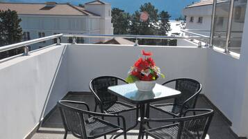 Uma varanda com mesa e cadeiras, um arranjo de flores e vista para edifícios e montanhas.