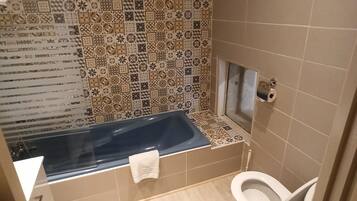 Casa de banho com banheira, sanita e azulejos estampados.