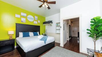 Quarto moderno com cama, mesa de cabeceira, relógio de parede e ventilador de teto.