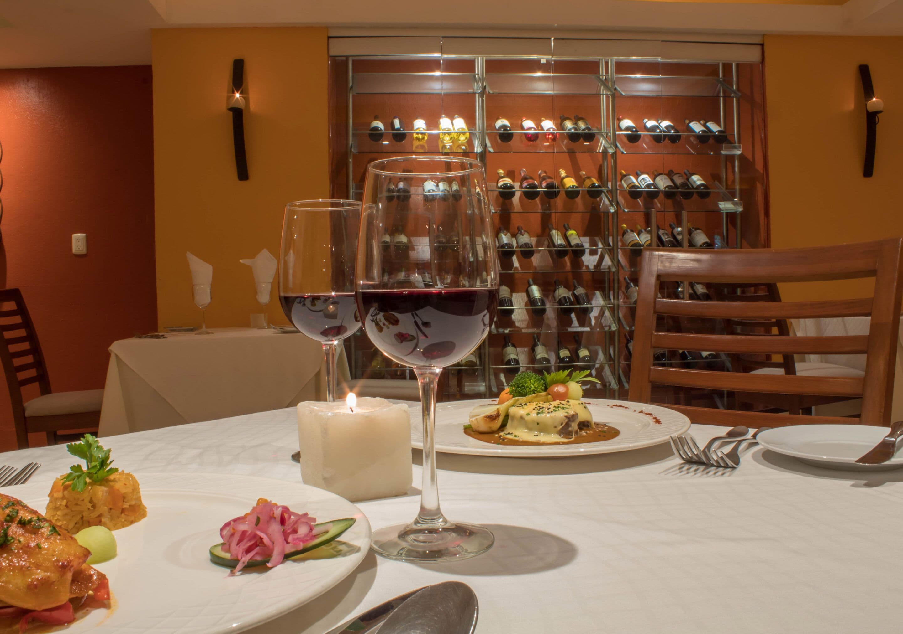Uma mesa de jantar com pratos de comida, copos de vinho e uma vela.