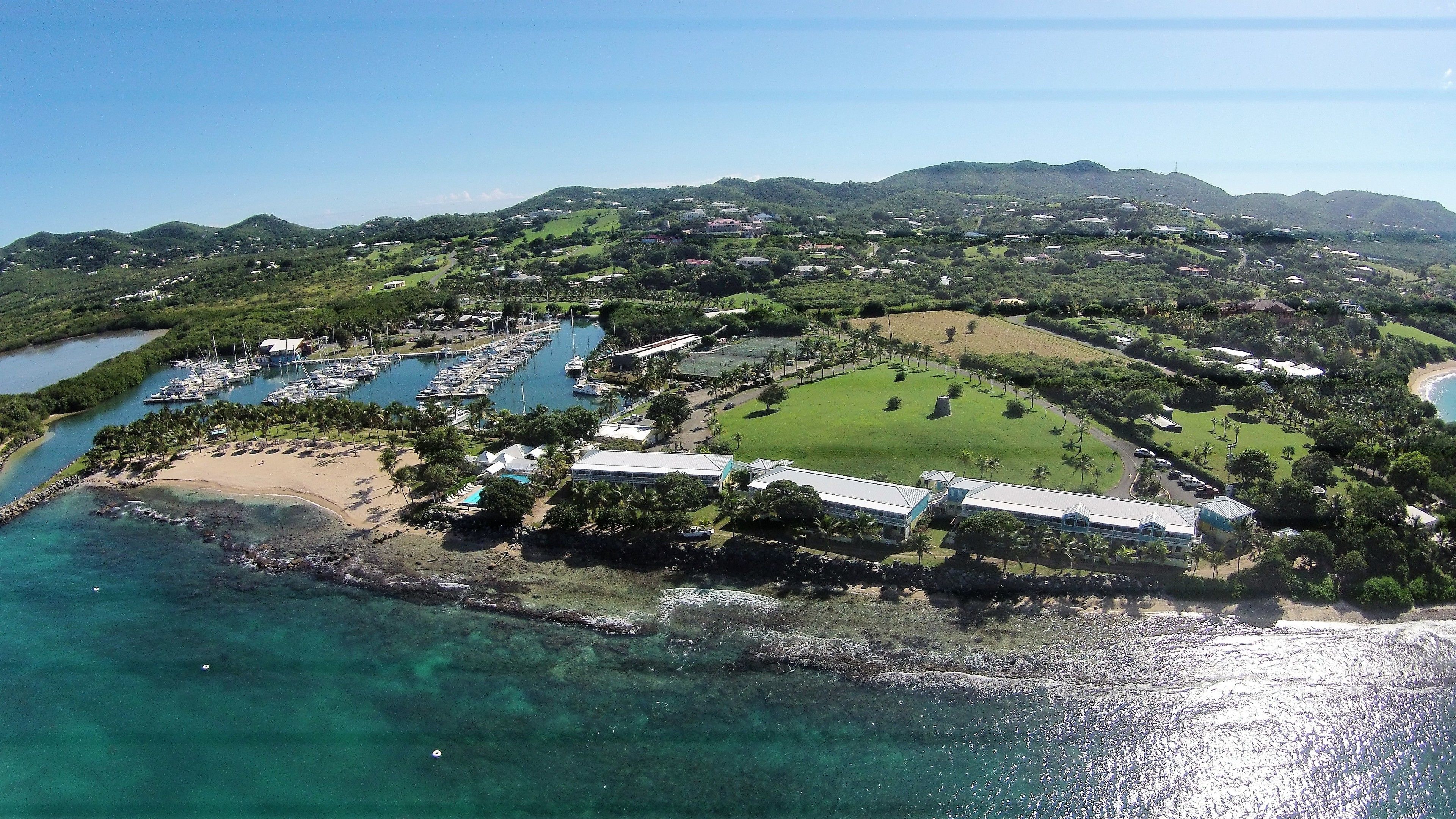 Vista aérea de um resort costeiro com marina, praia e vegetação exuberante.