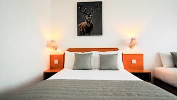 Quarto de hotel com uma cama grande, duas mesas de cabeceira, um quadro de veado fixado na parede e duas luminárias de parede.