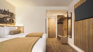 Quarto de hotel com duas camas, piso de madeira, um espelho e um quadro na parede.