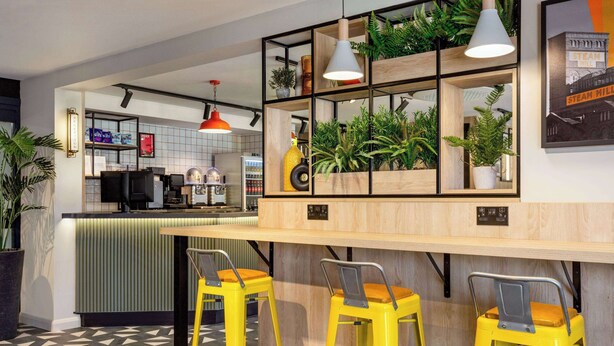 Uma área de bar com banquetas amarelas, balcão de madeira e plantas em vasos.