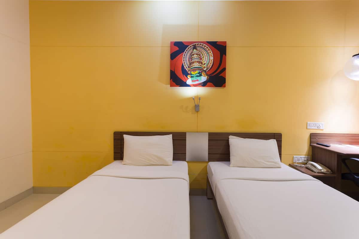 Quarto de hotel com duas camas, uma obra de arte na parede, uma mesa com telefone e uma luminária.