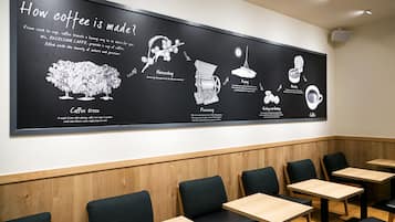 Um infográfico fixado na parede que explica o processo de preparo do café em um café, com mesas e cadeiras.