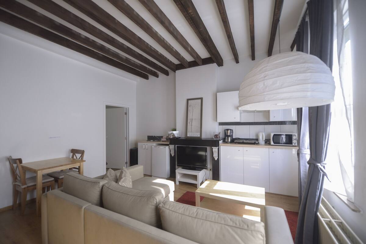 Um espaço compacto com sofá, mesa de jantar, cozinha compacta e uma grande janela com cortinas.