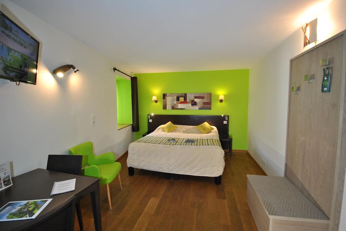 Quarto de hotel com cama, escrivaninha, cadeira e televisão.