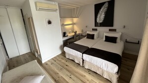 Quarto de hotel com duas camas, uma escrivaninha, uma cadeira, um guarda-roupa e uma grande obra de arte com penas na parede.