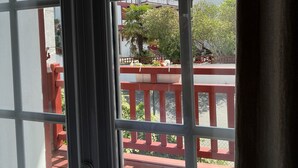 Vista pela janela, com grade de metal, mostrando uma varanda vermelha com corrimão e plantas em vasos.