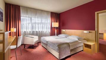 Quarto de hotel com cama, escrivaninha, cadeira e janela com cortinas.