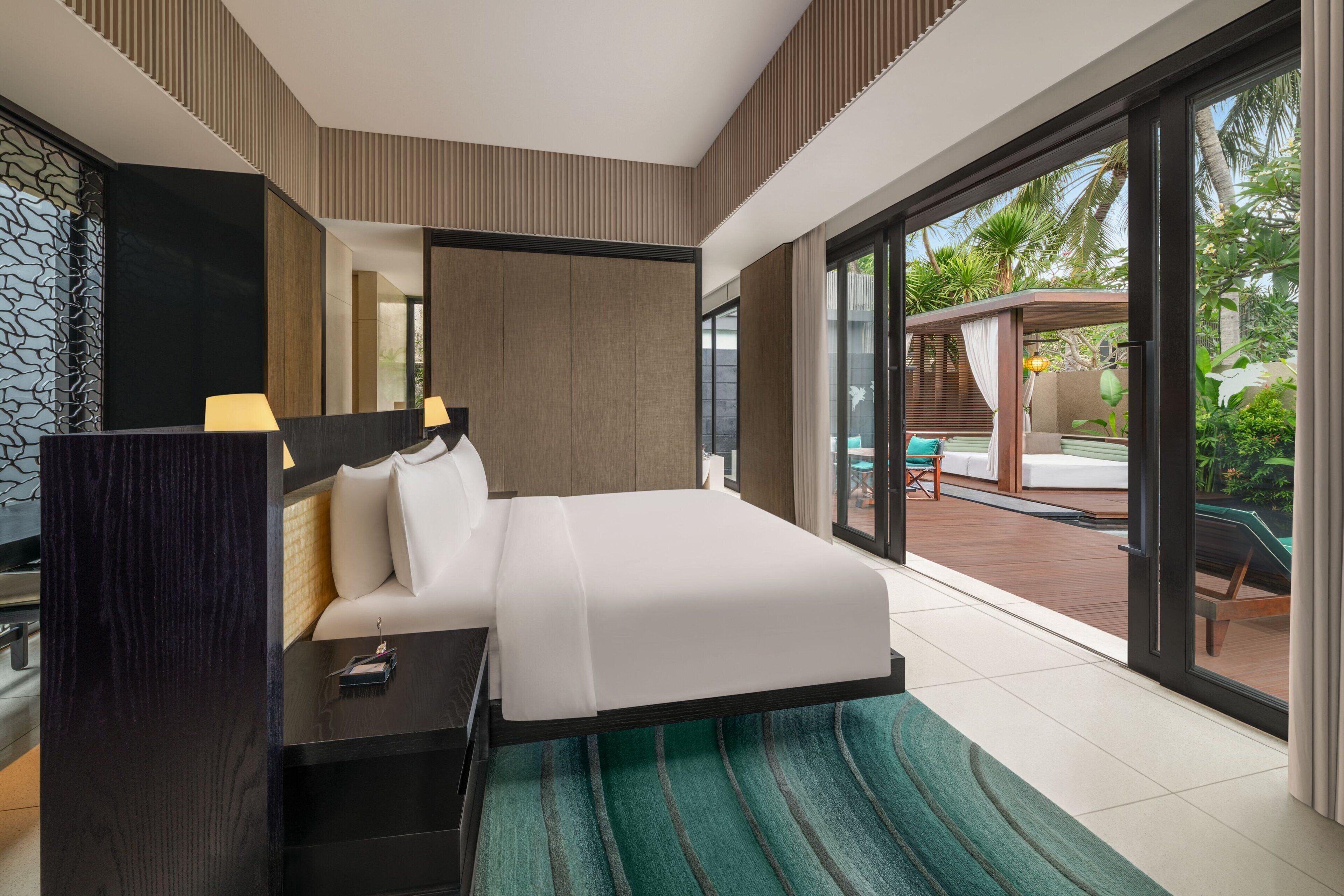 Quarto de hotel moderno com uma cama grande, uma escrivaninha e vista para a piscina e jardim.