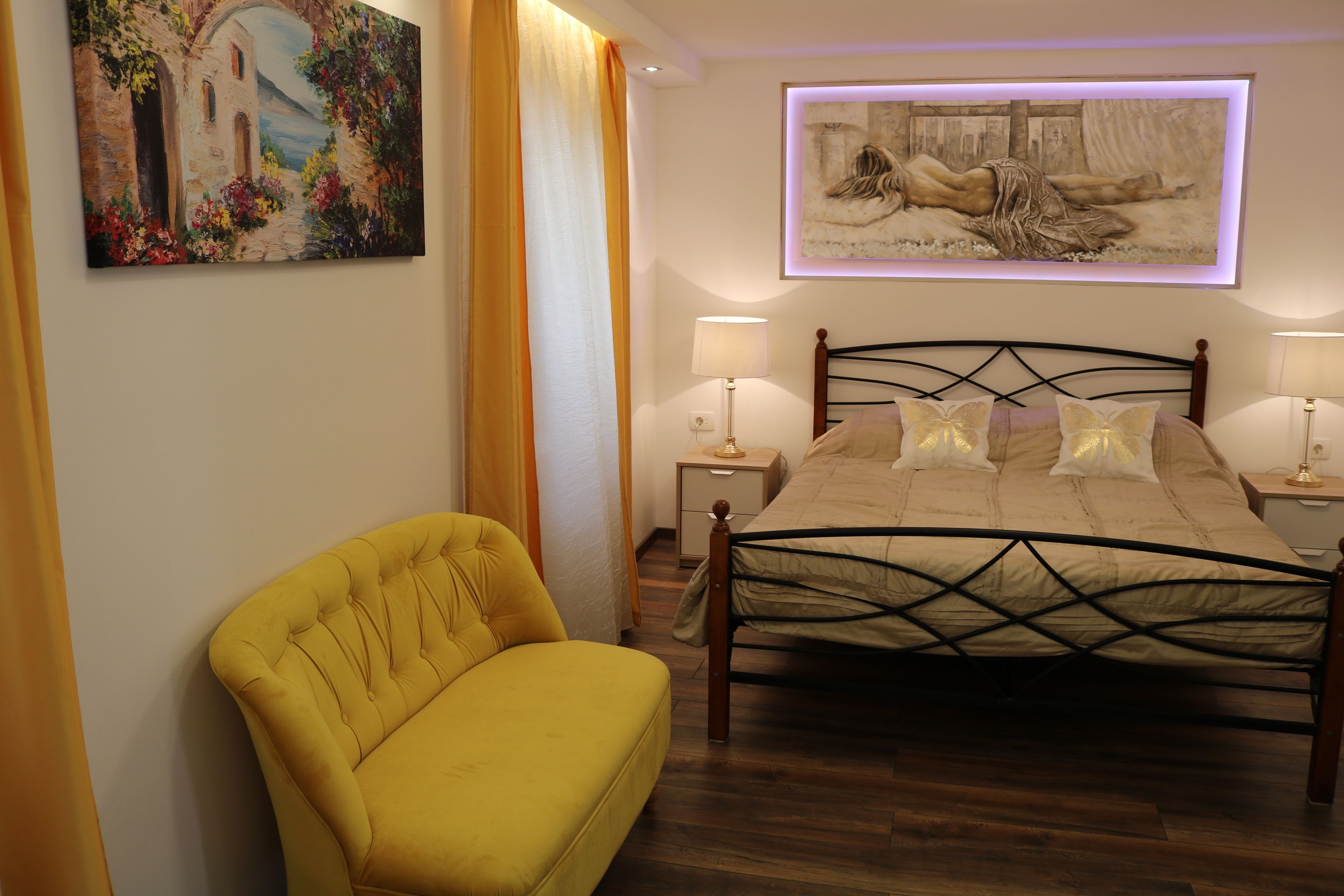 Quarto com cama, poltrona amarela, pintura e uma obra de arte na parede.