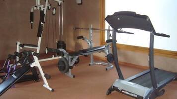 Uma academia com diversos equipamentos de exercício, incluindo esteira, banco de musculação e aparelho multifuncional para treino.