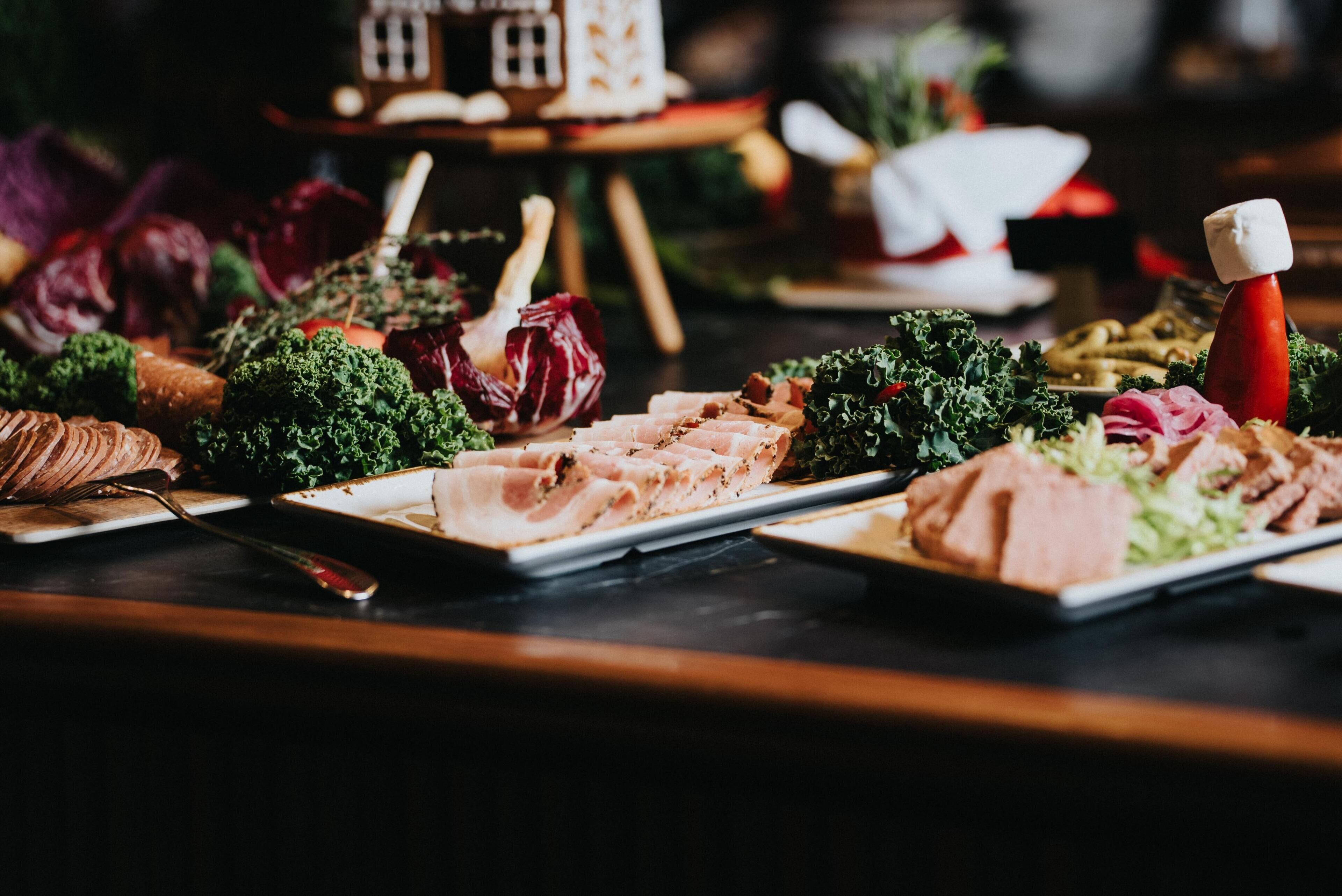 Uma mesa com diversos alimentos, incluindo carnes fatiadas e vegetais, preparada para uma refeição.