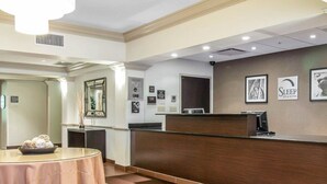 Uma área de recepção com um balcão de madeira, uma divisória de vidro e uma pequena mesa redonda com um objeto decorativo.