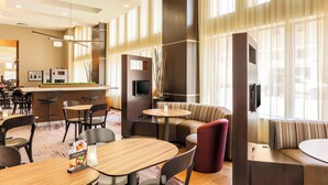 Um hall de hotel moderno com área de bar, assentos e grandes janelas que permitem entrada de luz natural.