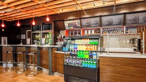 Uma área de bar com um dispensador de bebidas, banquetas e um quadro de cardápio.