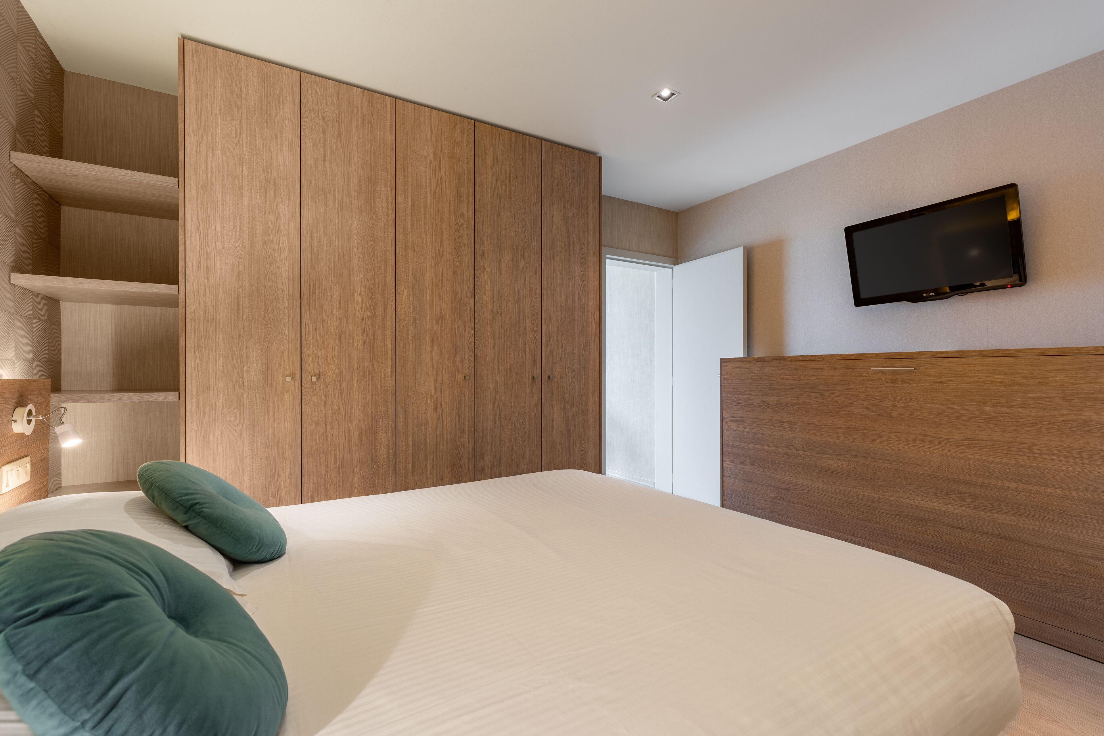 Quarto moderno com cama, televisão fixada na parede e estantes de madeira embutidas.