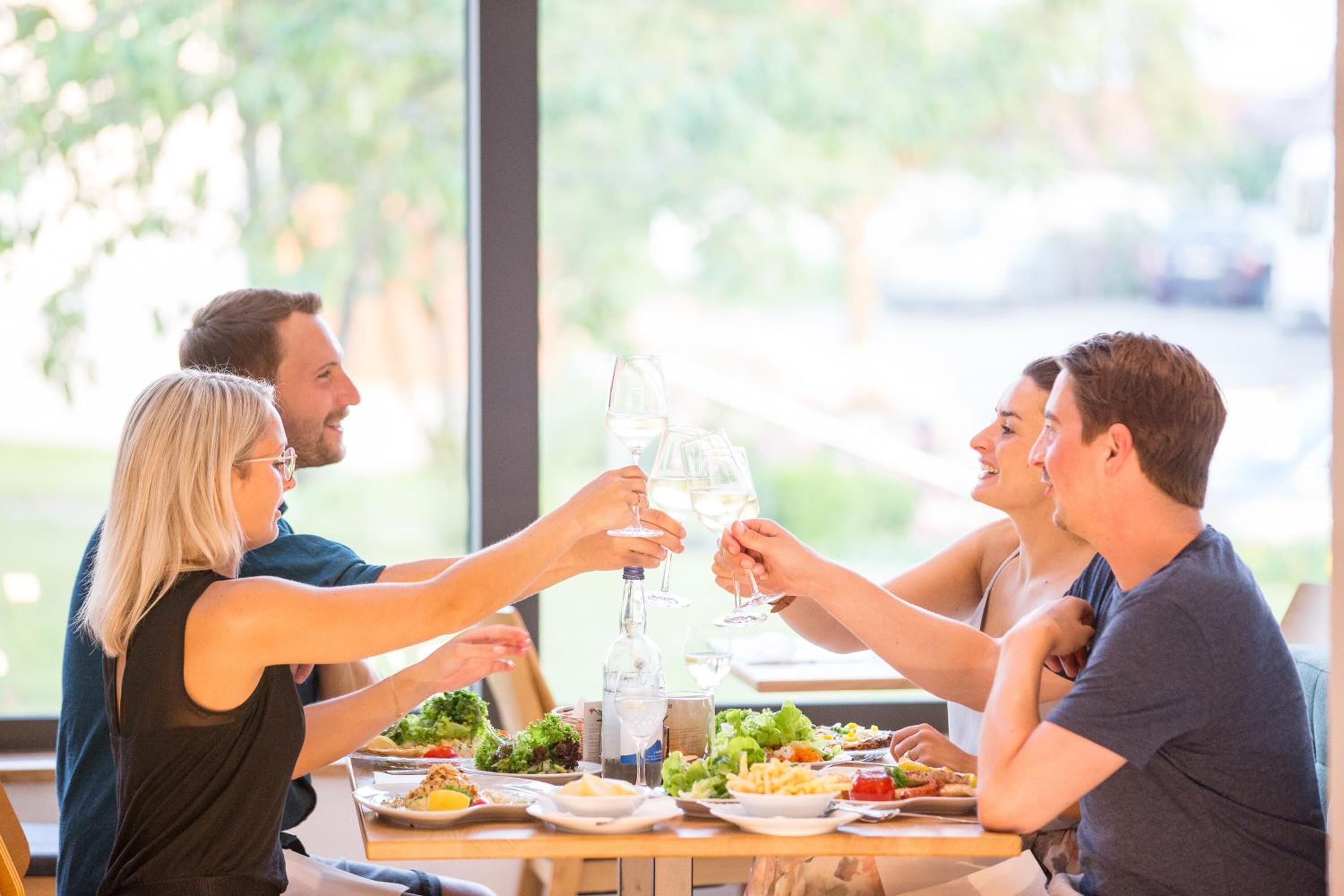 Um grupo de pessoas brindando com taças de vinho à mesa, com diversos pratos.