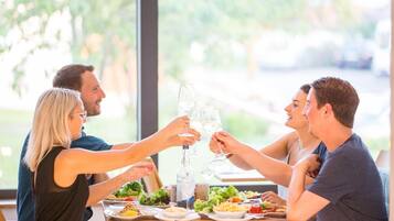 Um grupo de pessoas brindando com taças de vinho à mesa, com diversos pratos.