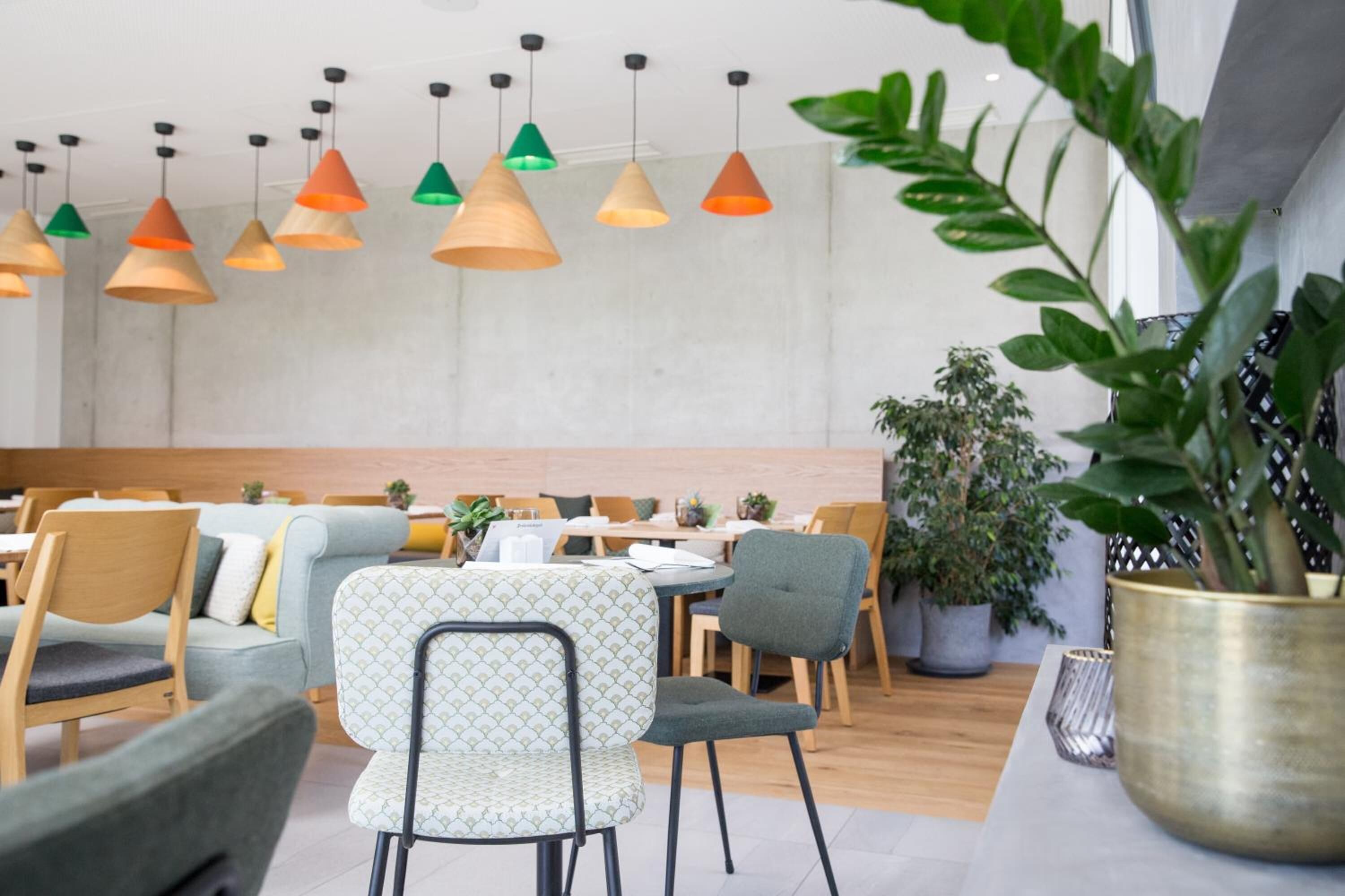 Uma sala de jantar moderna com várias mesas e cadeiras, luminárias pendentes coloridas e plantas em vasos.