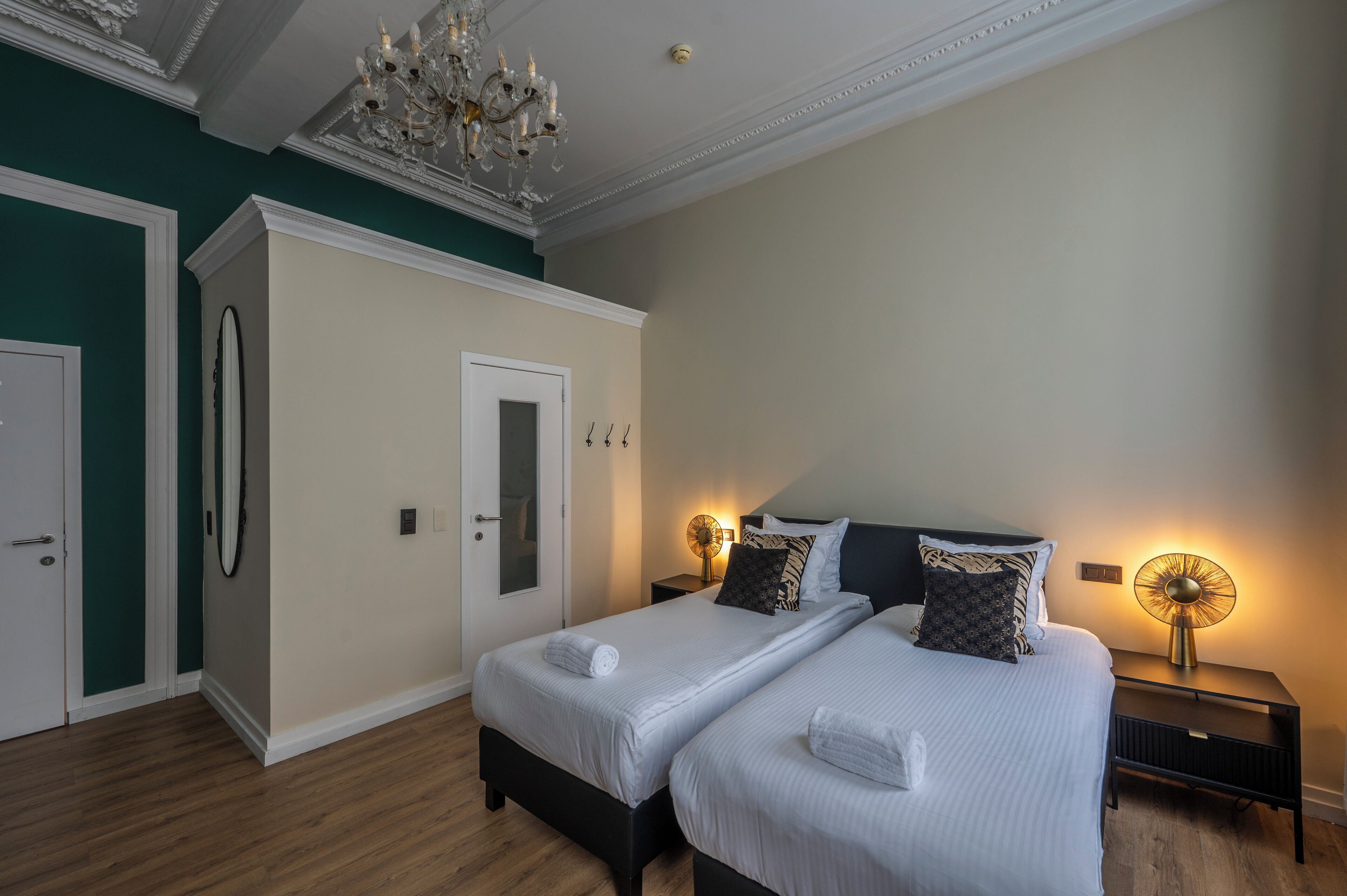 Quarto com duas camas, um candelabro, luminárias de cabeceira e um guarda-roupa.