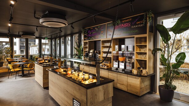Um café moderno com móveis de madeira, um balcão central com comida e estantes com produtos.