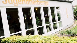 Um edifício com a inscrição 'Jugendherberge' na fachada, com grandes janelas e um jardim na frente.