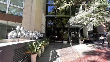 Entrada de hotel com uma placa chamativa, plantas em vasos e uma cobertura.