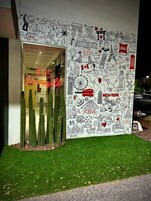 Entrada de hotel com uma placa de neon indicando "ibis Hermosillo" e uma parede decorada com desenhos temáticos de viagens.