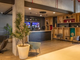 Uma área de recepção moderna com um balcão de madeira, duas televisões e uma grande planta em vaso.