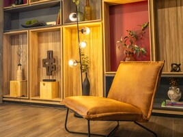 Uma sala de estar moderna com piso de madeira, uma poltrona de couro marrom, uma estante de madeira e uma parede em destaque vermelha.