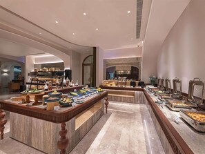 Uma área de buffet com vários pontos de comida e uma cozinha ao fundo.