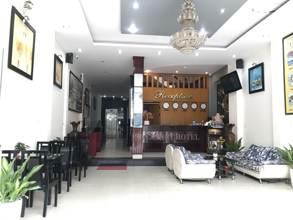 Uma área de recepção de hotel, com balcão, espaço para sentar e um lustre.
