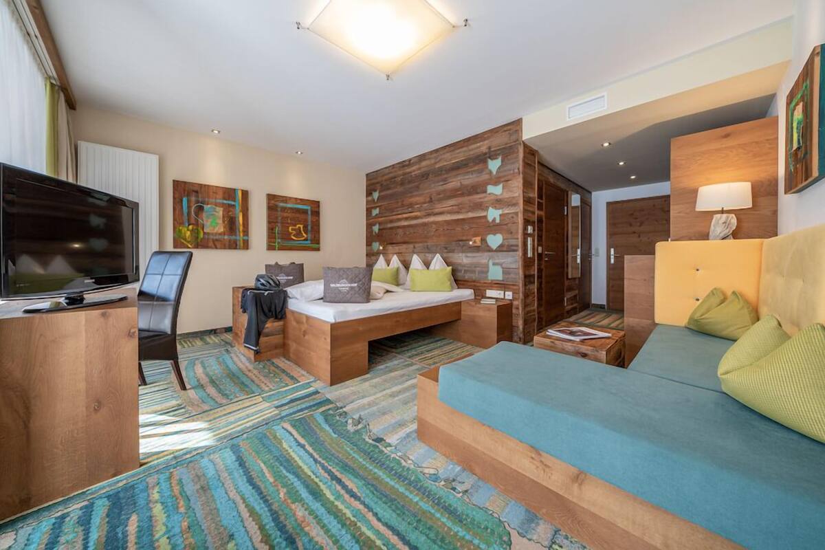 Quarto de hotel moderno com cama, sofá, escrivaninha e televisão.