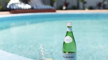 Ambiente de piscina com uma garrafa de água Pellegrino e um copo com canudo.
