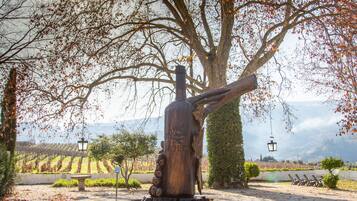 Uma escultura de madeira com um banco em um parque, com vinhedos ao fundo.