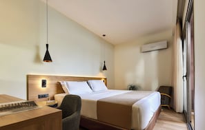 Quarto de hotel com cama, mesa de cabeceira, cadeira e escrivaninha.