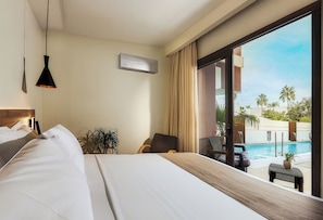 Quarto de hotel com uma cama grande, uma escrivaninha, uma cadeira, um vaso de plantas e vista para uma piscina.