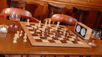Uma mesa de madeira com um tabuleiro de xadrez, dois copos com líquido âmbar e um relógio.