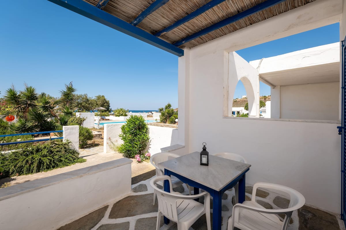 Uma varanda com mesa e cadeiras, com vista para uma praia e edifícios brancos.