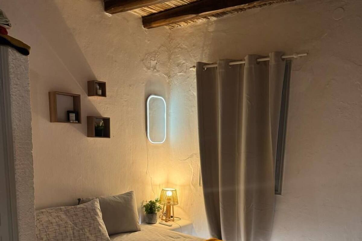 Quarto com cama, mesa de cabeceira, abajur e janela com cortinas.