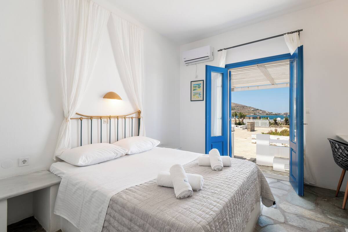 Quarto com cama, mesa de cabeceira, abajur e vista para o exterior.