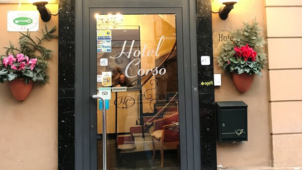 Entrada de hotel com porta preta, iluminada por arandelas e decorada com luzes de Natal.
