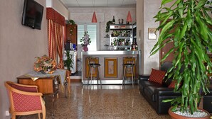 Uma sala de estar com sofá, uma mesa de jantar com cadeiras, área de cozinha com balcão e uma planta grande em vaso.